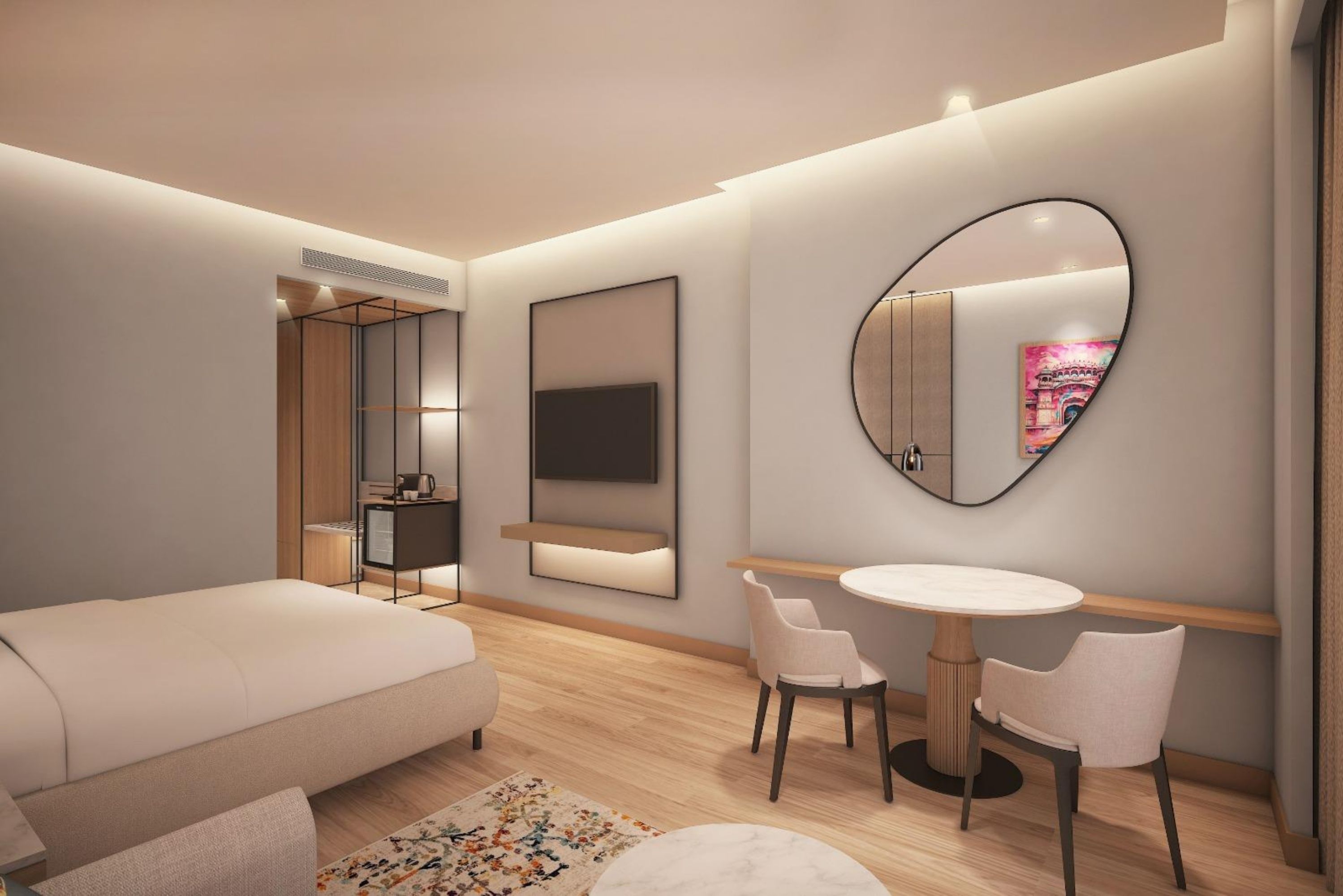 Quarto de hotel moderno com cama, televisão, espelho redondo, pequena mesa com cadeiras e cozinha compacta.