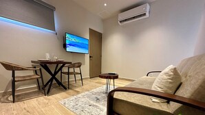 Uma sala de estar moderna com sofá, mesa de jantar com cadeiras, TV e aparelho de ar condicionado.