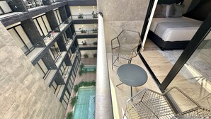 Um edifício alto com várias varandas, uma piscina e um quarto com cama e poltrona.