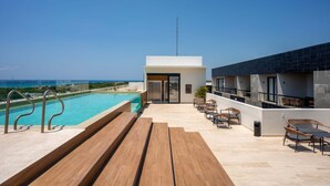Uma área de piscina no terraço com vista para o oceano, bancos de madeira e assentos externos.