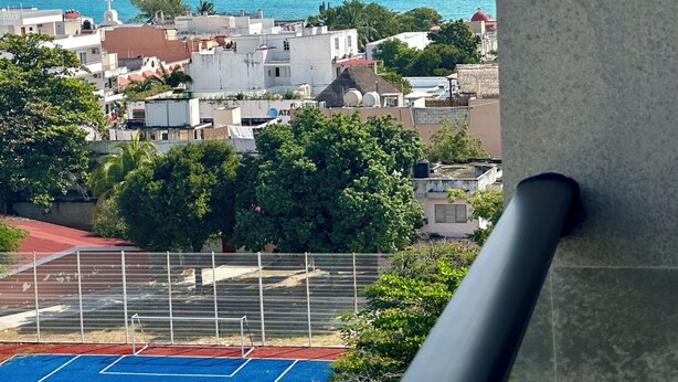 Uma vila costeira com edifícios, um campo esportivo e vista para o mar.