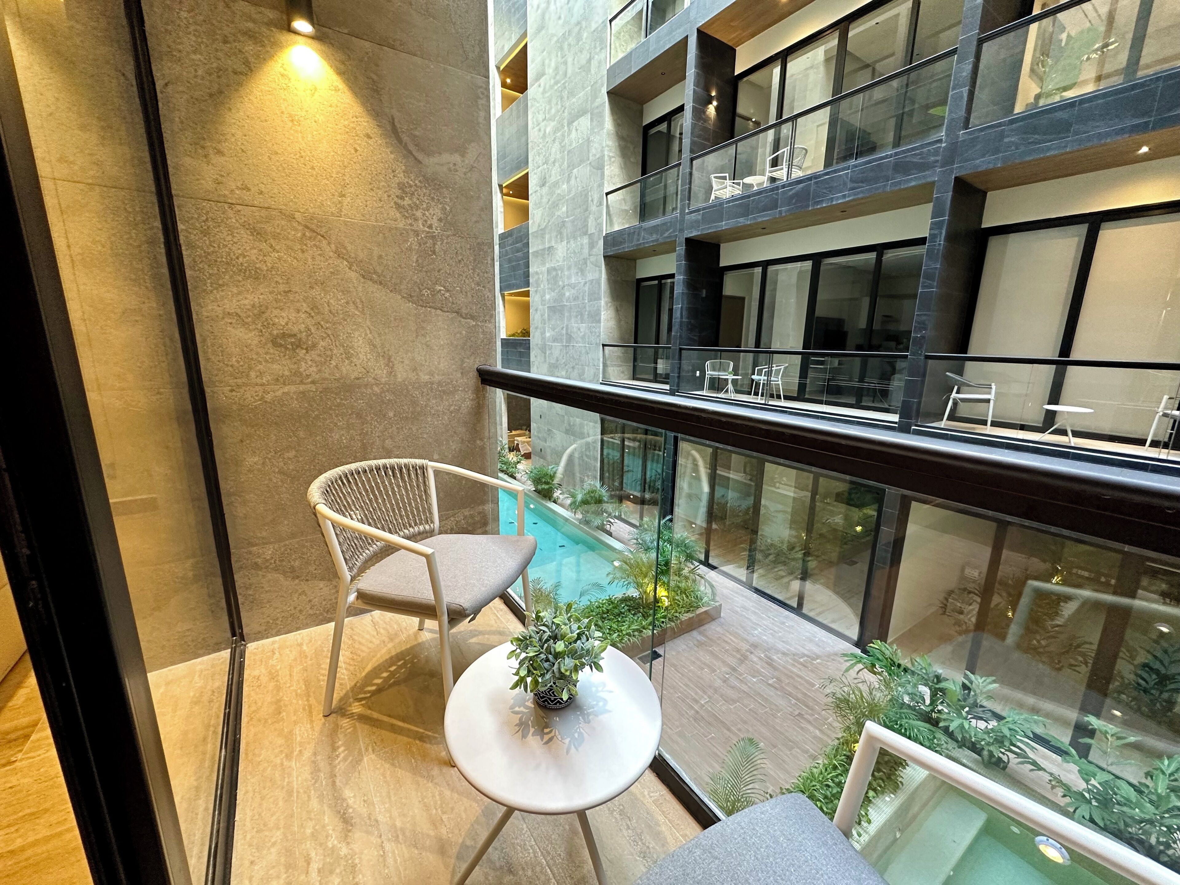 Interior moderno de hotel com balaustrada de vidro, piscina e área de estar com cadeira e mesa.