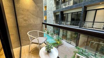 Interior moderno de hotel com balaustrada de vidro, piscina e área de estar com cadeira e mesa.