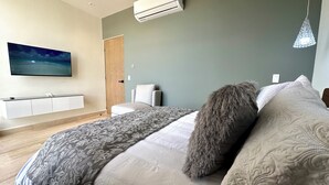 Um quarto moderno com uma cama grande, uma TV na parede, um aparelho de ar condicionado e uma porta de madeira.