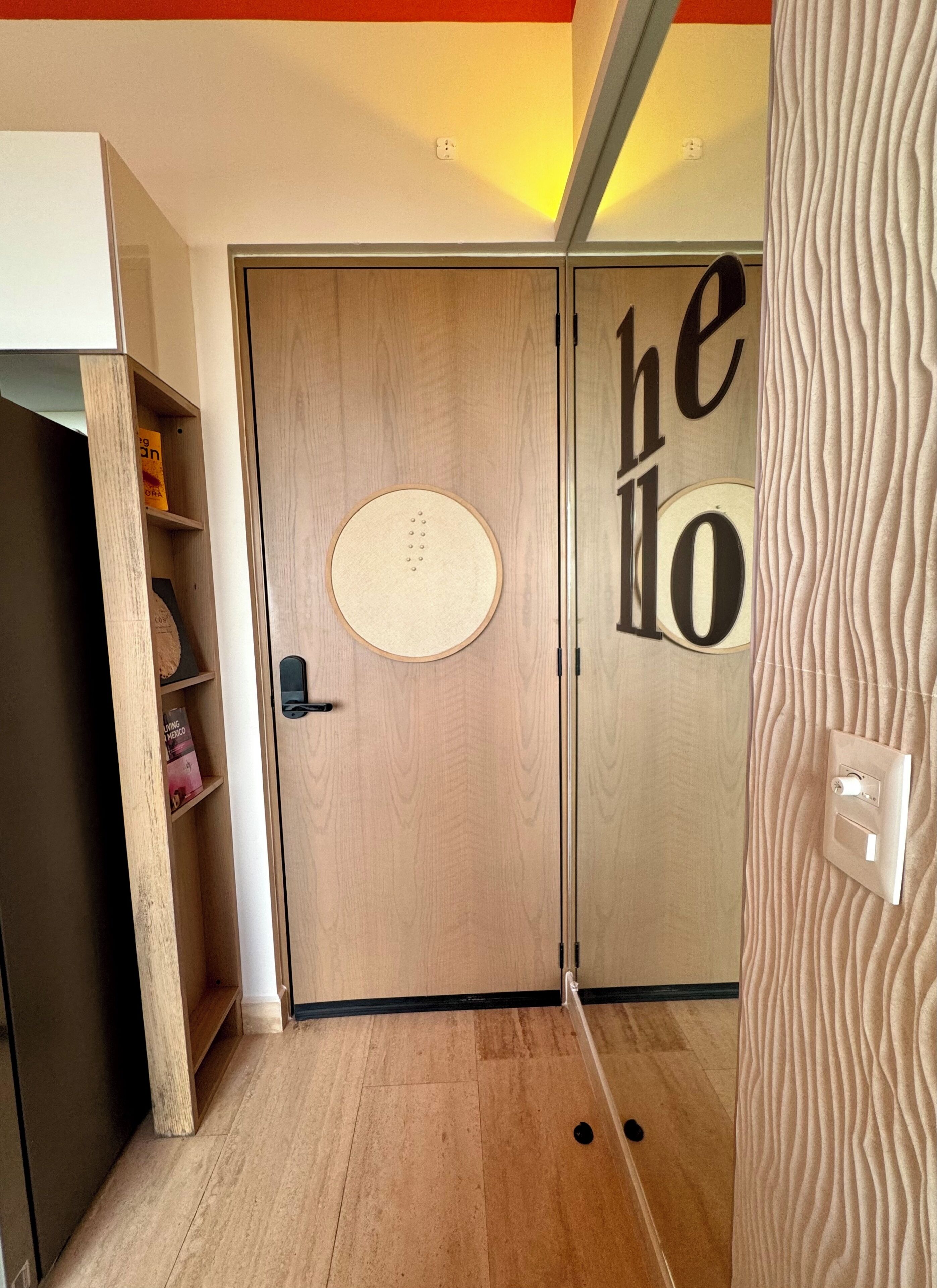 Uma porta de madeira com puxador circular, uma estante com livros e uma parede com textura.