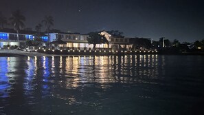 Um imóvel à beira-mar com edifícios iluminados, superfície aquática refletora e palmeiras.