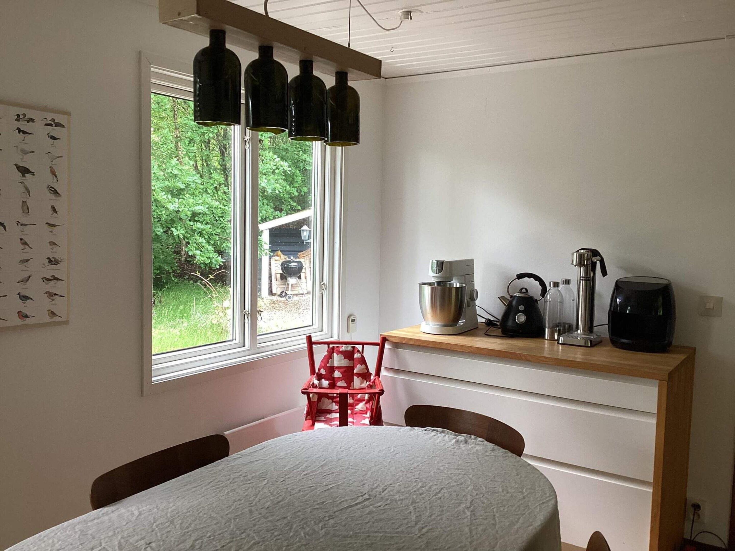 Cozinha com bancada de madeira, uma cadeira vermelha, mesa branca e janela com vista para o verde.