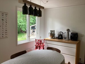 Cozinha com bancada de madeira, uma cadeira vermelha, mesa branca e janela com vista para o verde.