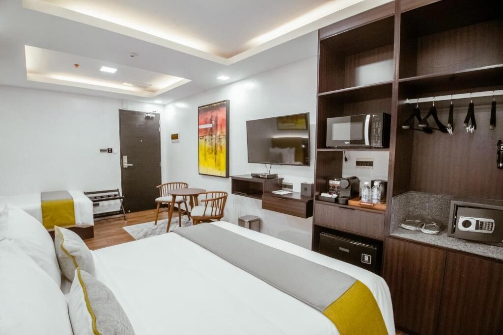 Quarto de hotel com cama, escrivaninha, cadeira, micro-ondas e cabideiro.