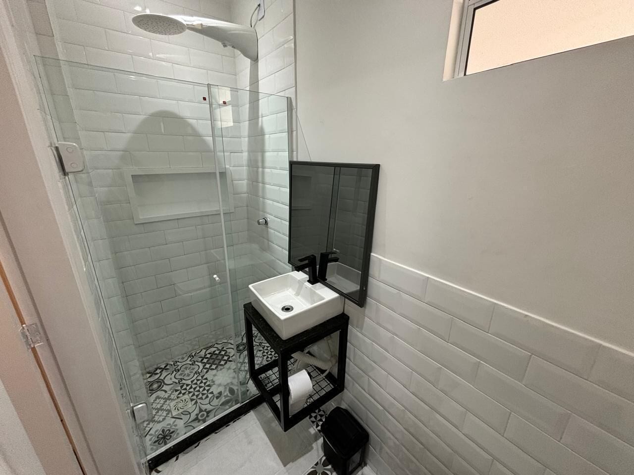 Casa de banho com chuveiro em cabine de vidro, pia branca, toucador preto e espelho.