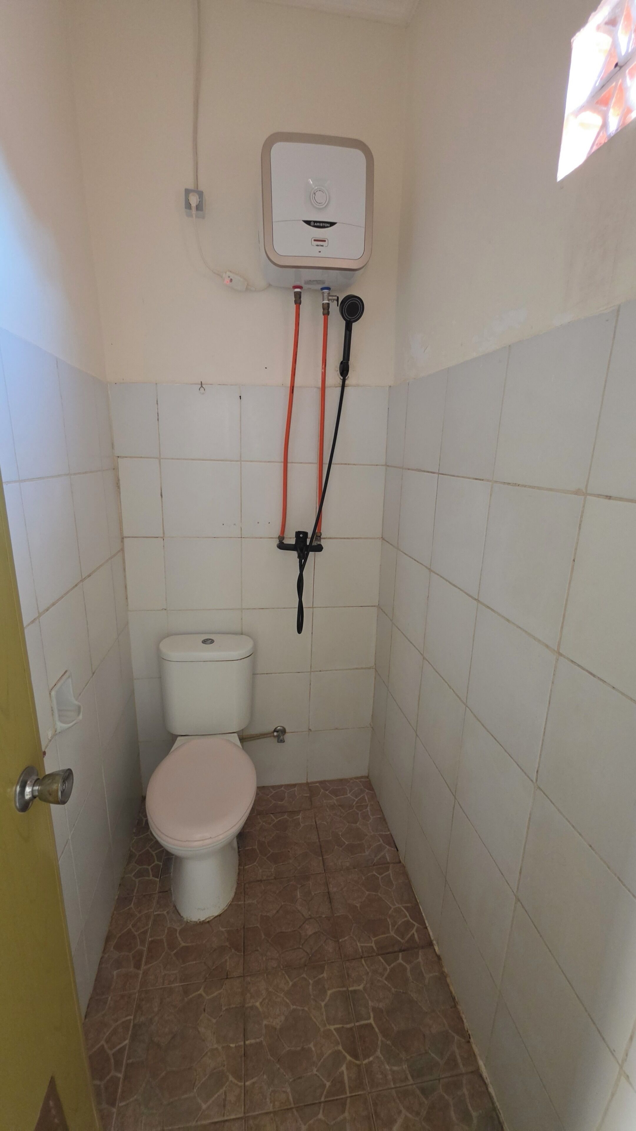 Um banheiro pequeno e revestido com azulejos, com vaso sanitário, aquecedor de água e chuveiro.