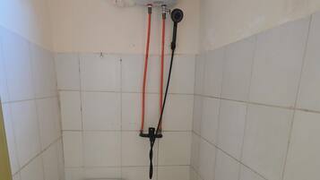 Um banheiro pequeno e revestido com azulejos, com vaso sanitário, aquecedor de água e chuveiro.