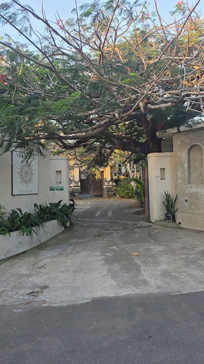 Entrada de uma propriedade com portão, placa indicando 'Eco-Lodge' e caminho pavimentado que leva à entrada.