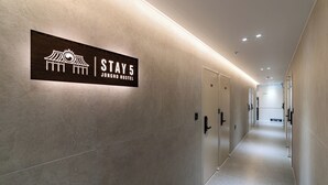 Um corredor com uma placa indicando 'STAY 5 JONGNO HOSTEL' e portas que dão para os quartos.
