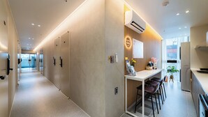 Um corredor moderno de hotel com balcão de recepção, cadeiras e uma pequena área de kitchenette.