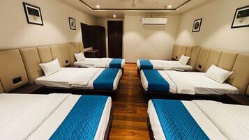 Quarto de hotel com quatro camas dispostas em linha, piso de madeira e um aparelho de ar condicionado na parede.