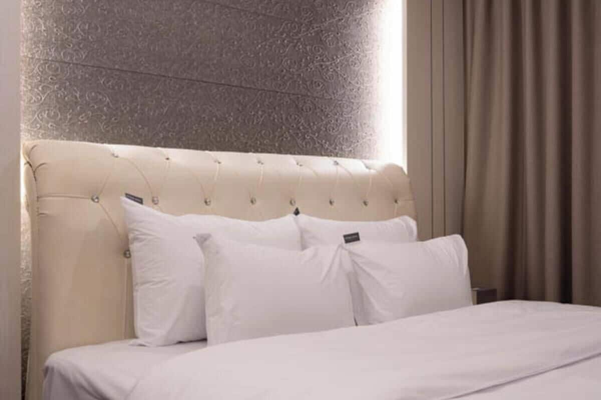 Cama com cabeceira estofada, roupa de cama branca e parede com textura.