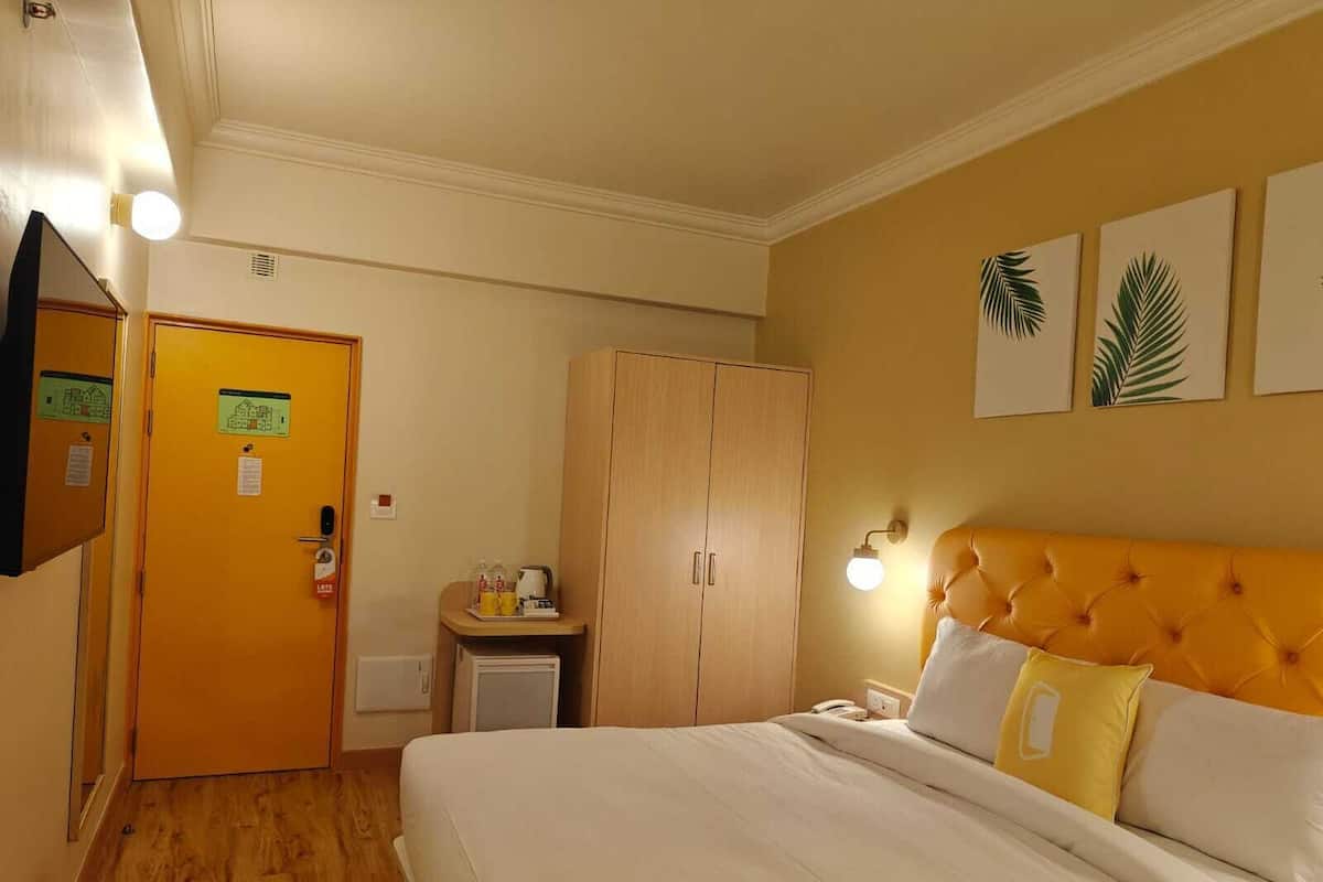 Quarto de hotel com cama, guarda-roupa, uma pequena mesa com chaleira e luminária fixada na parede.