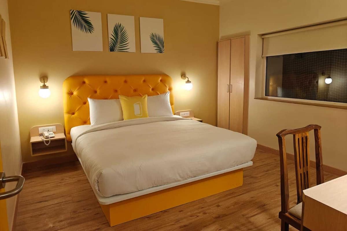 Quarto de hotel com cama, mesa de cabeceira, luminária e janela com vista.