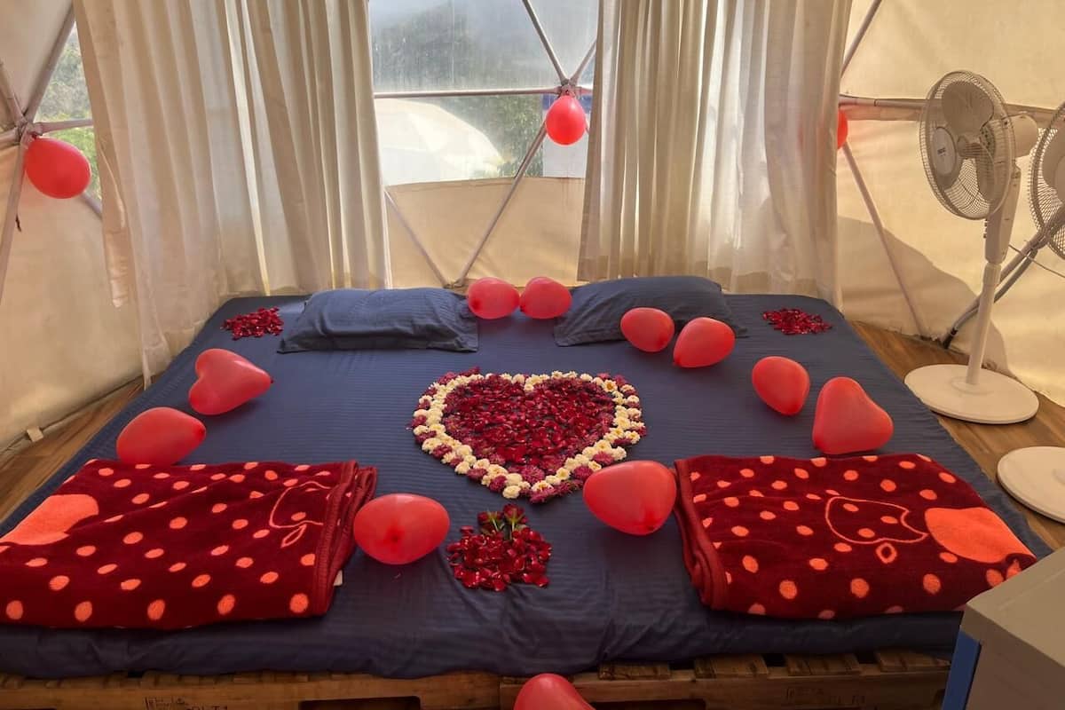 Um quarto com tenda, uma cama, decorações em formato de coração vermelho e balões.