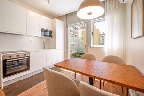 Uma cozinha moderna com armários brancos, forno embutido e sala de jantar com mesa e cadeiras de madeira.