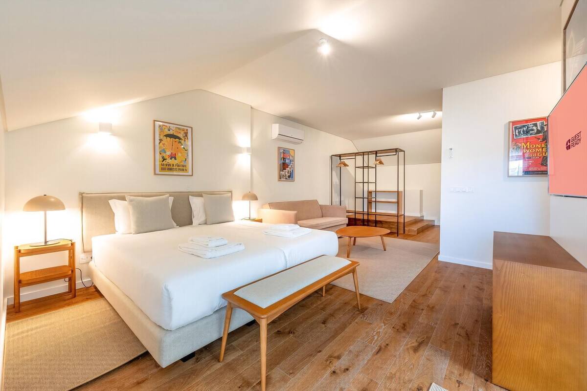 Um quarto com uma cama, mesas de cabeceira, um banco, um sofá e uma pequena mesa.