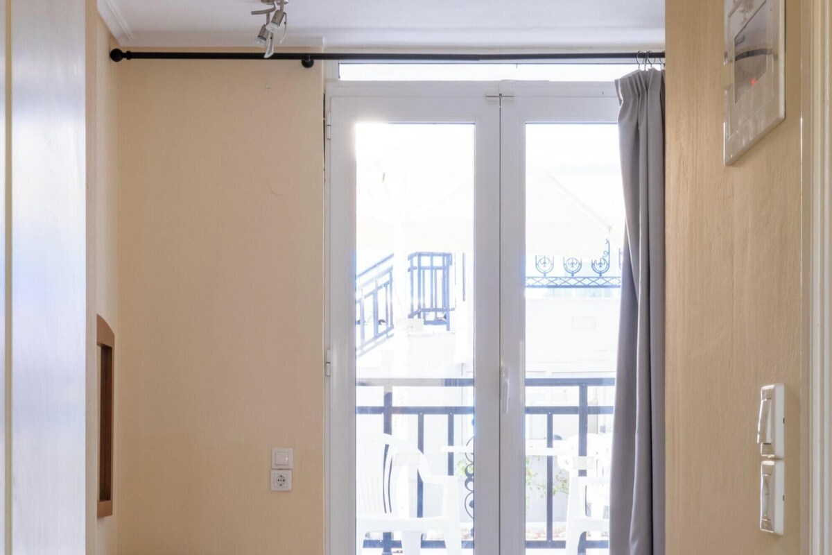 Quarto de hotel com cama, escrivaninha e janela com vista para uma varanda.
