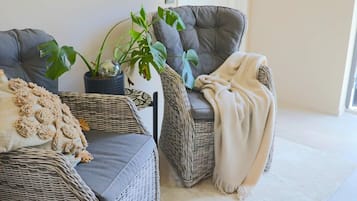 Quarto com sofá cinza, cadeira de vime, planta em vaso e manta.