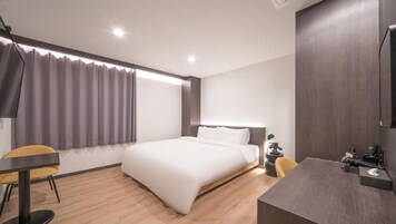 Quarto de hotel moderno com uma cama grande, uma escrivaninha, uma cadeira e uma pequena mesa com comodidades.