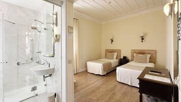 Quarto de hotel com banheiro, duas camas, escrivaninha e espelho.