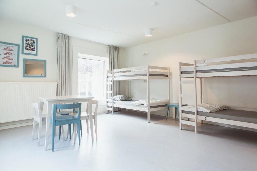 Um dormitório com beliches, uma escrivaninha, cadeiras e uma janela.