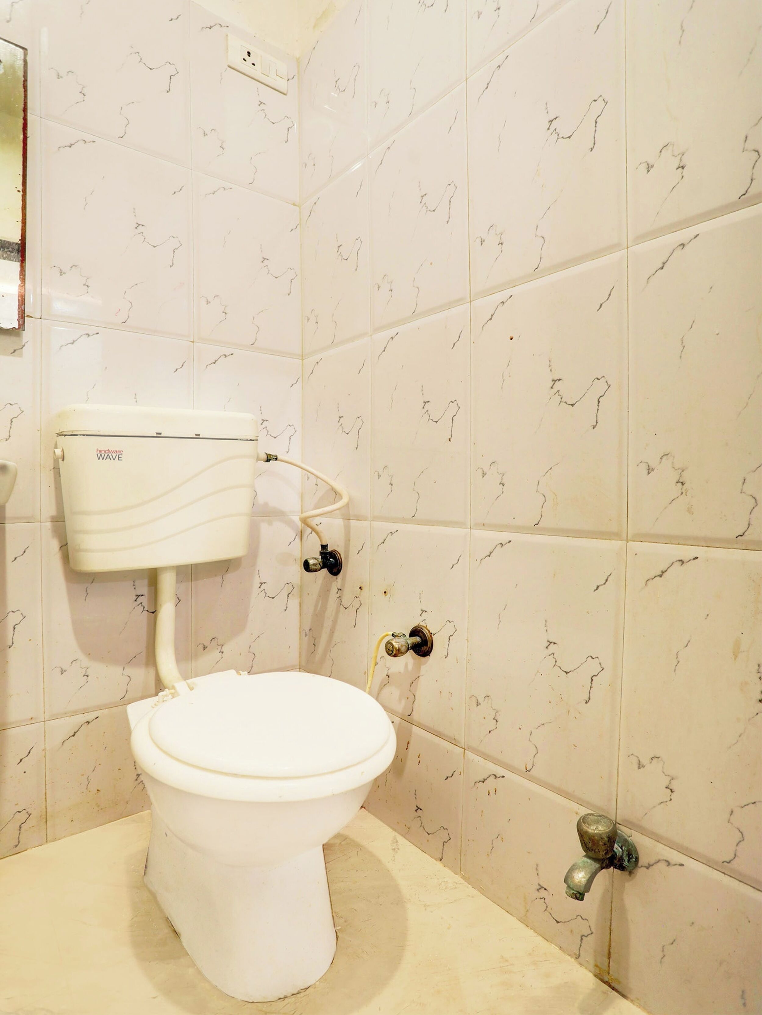 Uma casa de banho com sanita, um ponto de água visível e um sistema de descarga na parede.