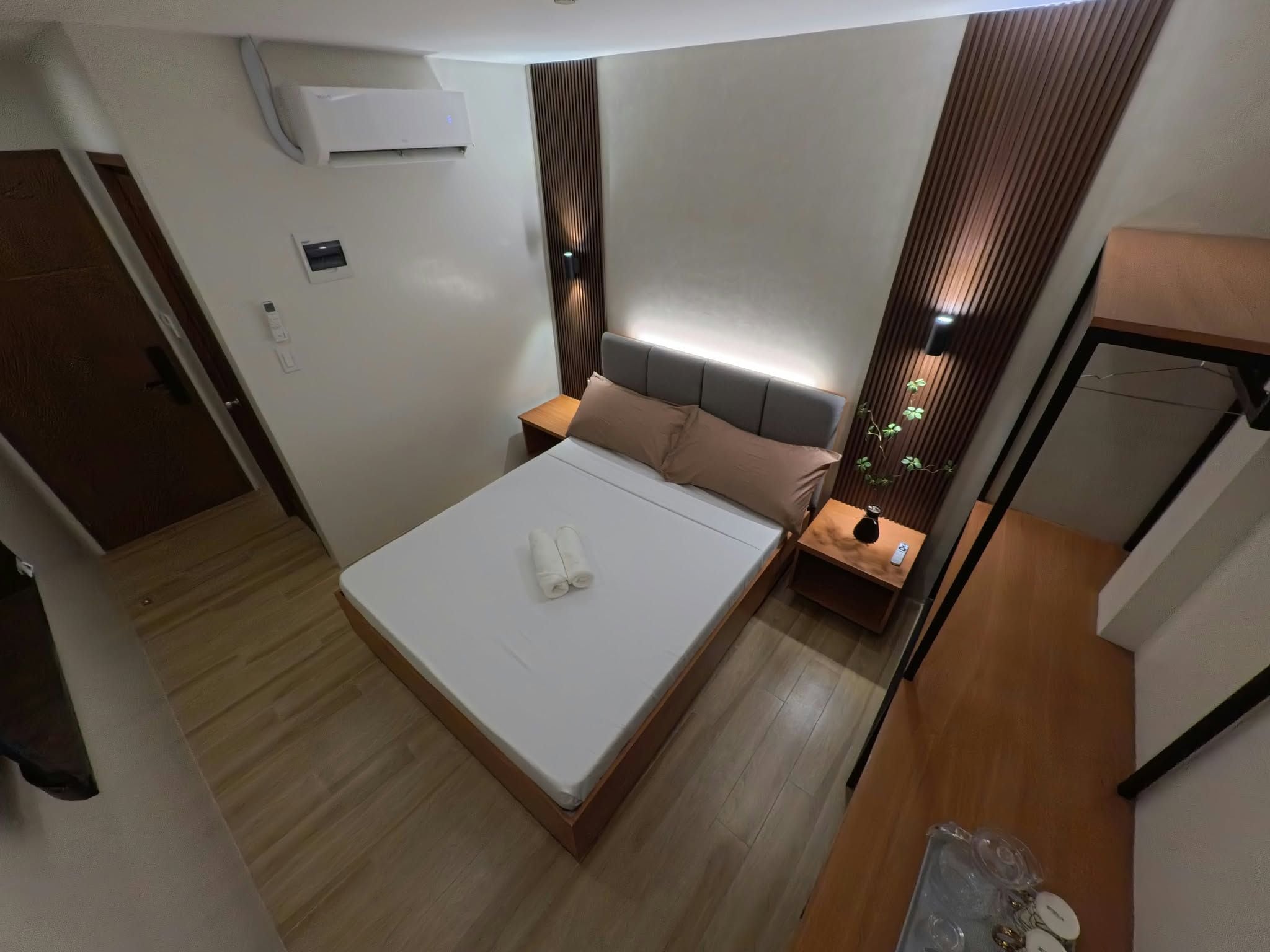 Quarto de hotel pequeno, com cama, mesas de cabeceira, guarda-roupa e ar condicionado.
