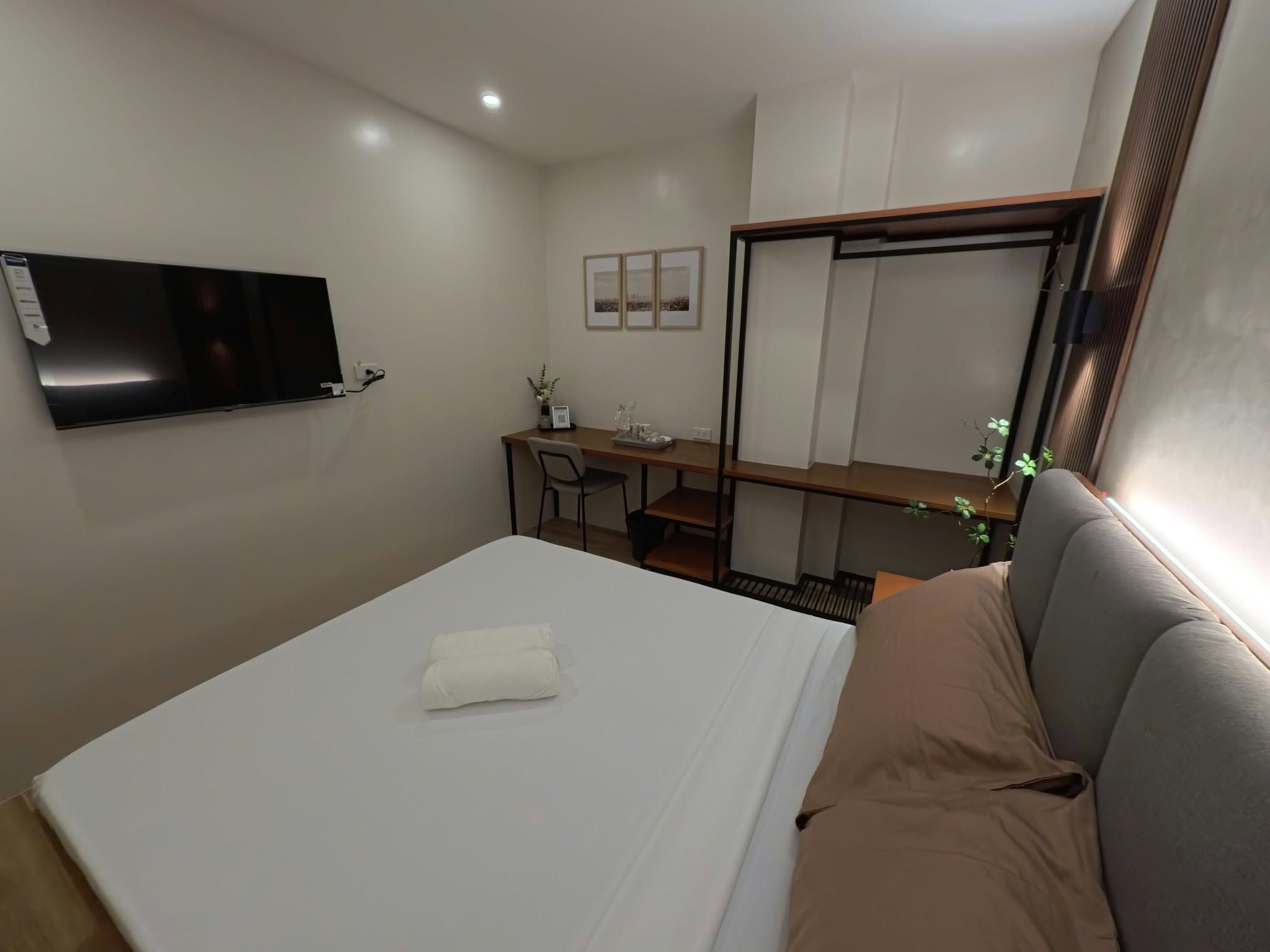 Quarto de hotel com cama, escrivaninha, cadeira, televisão e espelho.