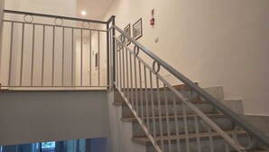 Uma escadaria com corrimão de metal, uma luminária no teto e um alarme de incêndio na parede.