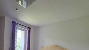 Quarto de hotel com cama, mesa de cabeceira, janela com cortinas e uma luminária no teto.