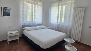 Quarto com uma cama, uma mesa de cabeceira, um radiador e um ventilador de teto.