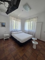 Quarto com uma cama, uma mesa de cabeceira, um radiador e um ventilador de teto.