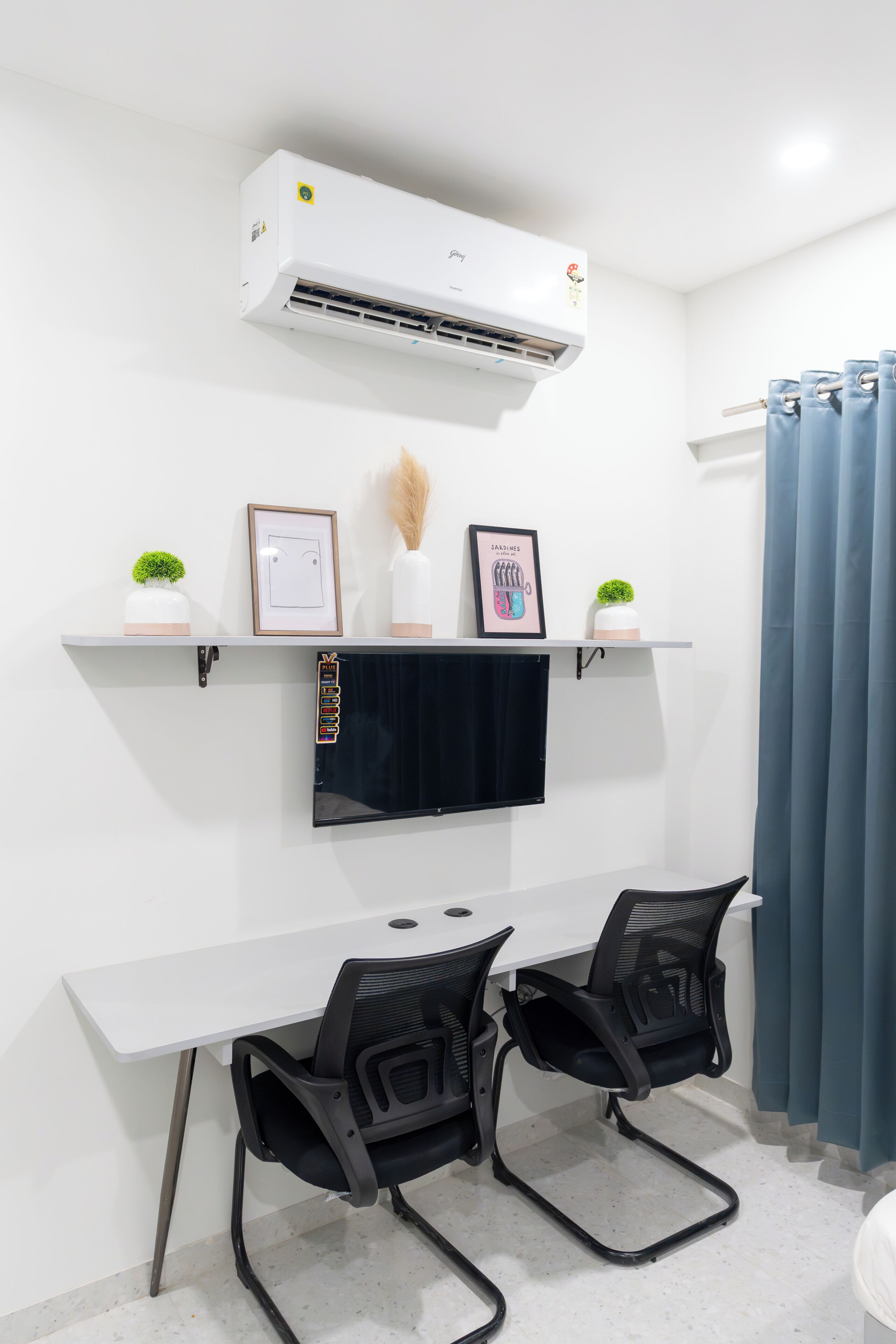 Um espaço de escritório moderno, com uma mesa branca, duas cadeiras de escritório pretas, uma TV fixada na parede e um aparelho de ar condicionado.