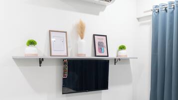 Um espaço de escritório moderno, com uma mesa branca, duas cadeiras de escritório pretas, uma TV fixada na parede e um aparelho de ar condicionado.