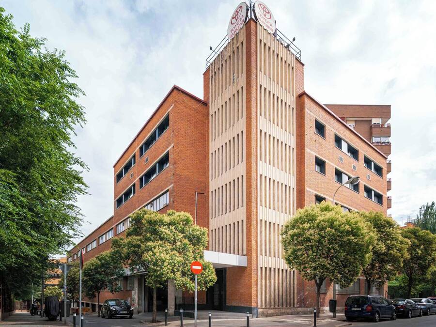 Um edifício de vários andares com um logotipo Toyota bem visível no topo, uma placa de proibido estacionar e árvores ao longo da rua.
