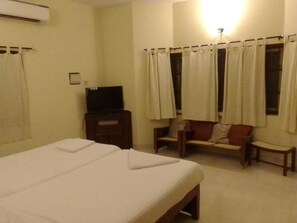 Quarto de hotel com cama, cómoda de madeira, televisão, sofá e janela com cortinas.