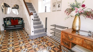 Uma escadaria com piso estampado, um sofá de couro preto, um armário de madeira e uma parede com quadros.