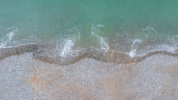 Uma praia com água cristalina e um areal de seixos.