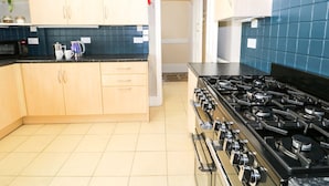Cozinha com armários de madeira clara, bancada preta, fogão com vários queimadores e backsplash de azulejos azuis.