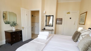 Quarto com cama grande, penteadeira, espelho, porta do banheiro e quadro na parede.