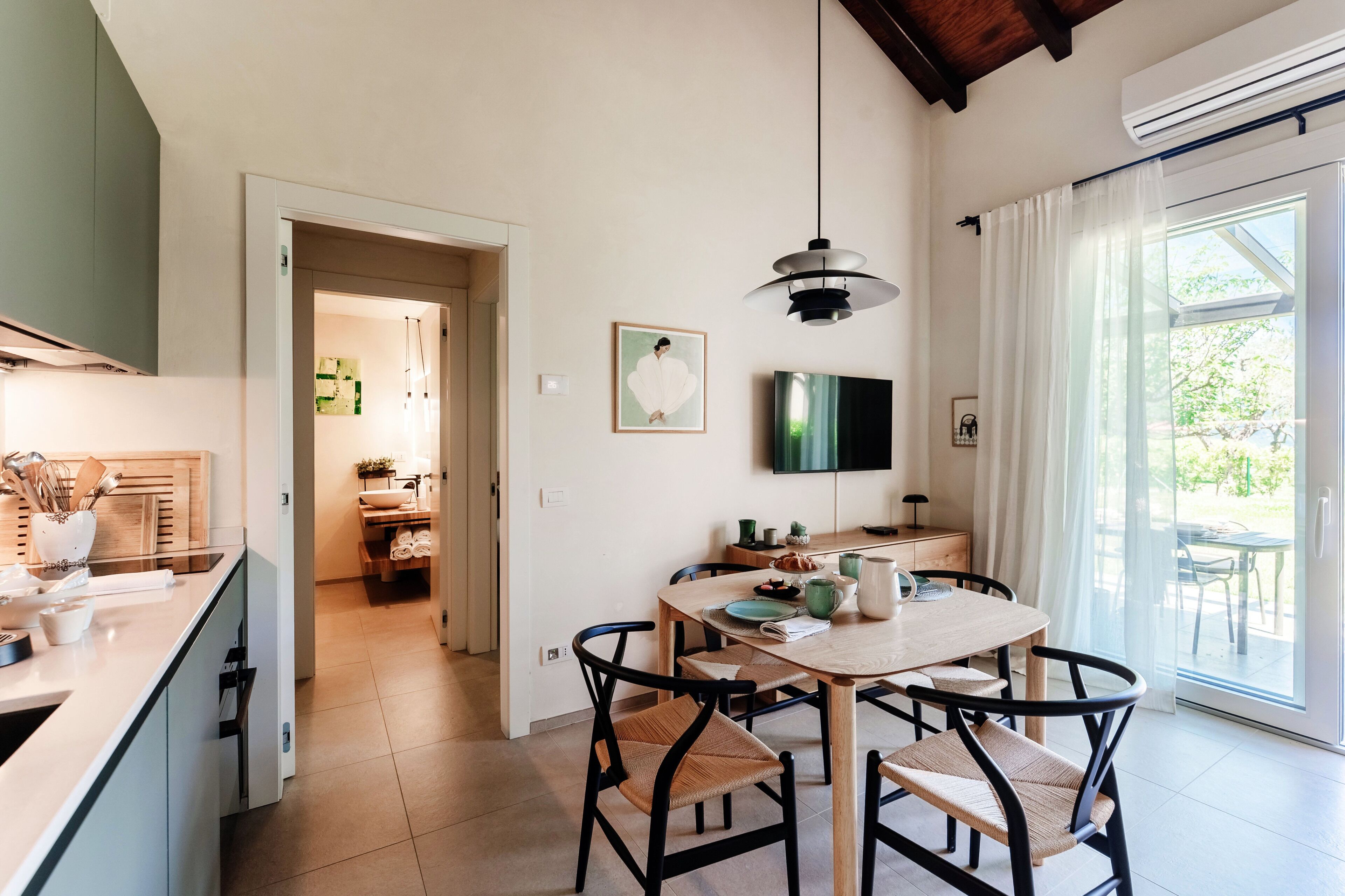 Cozinha moderna com área de refeições, com mesa de madeira, cadeiras pretas e luminária pendente.