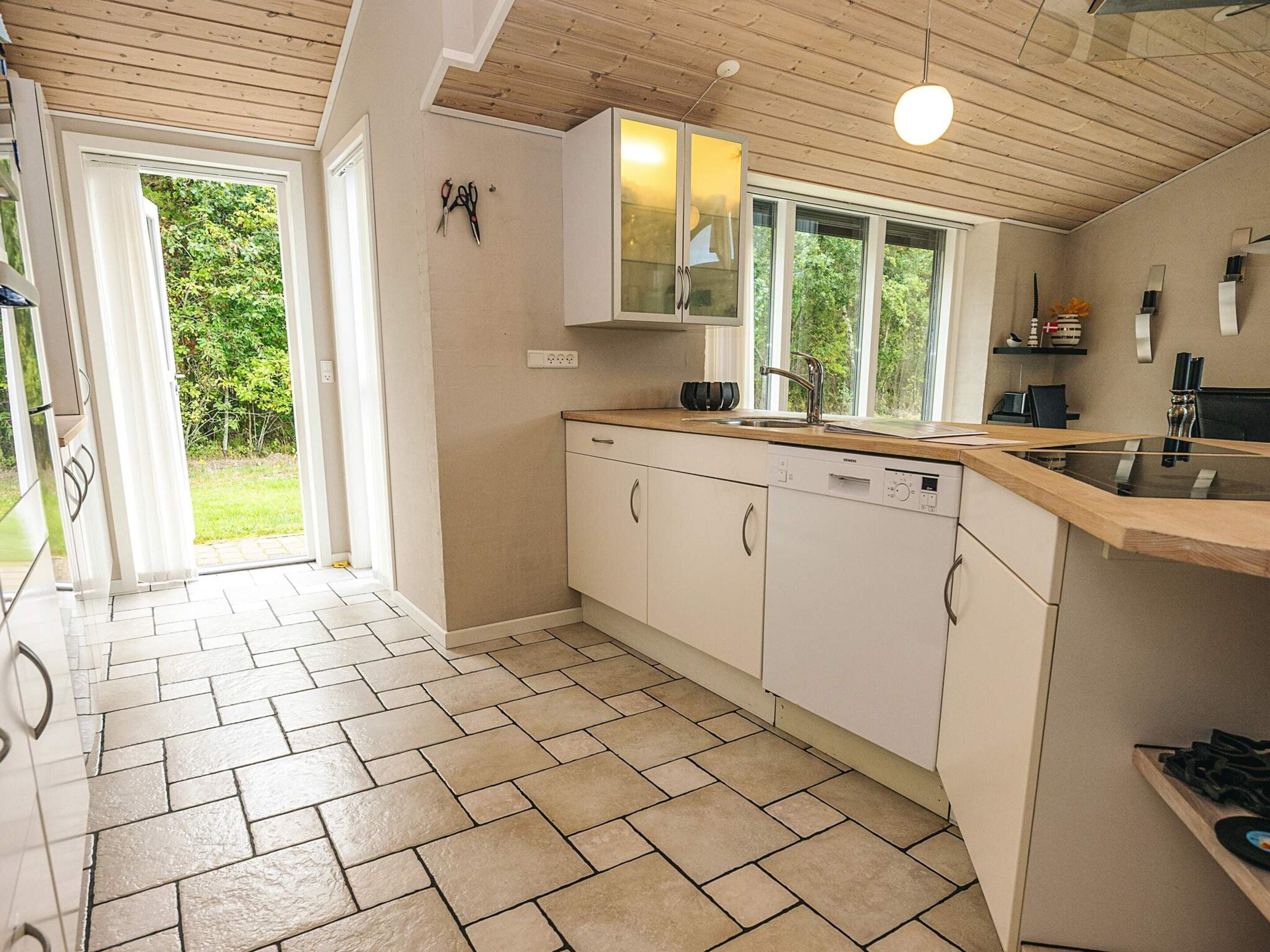Cozinha equipada com lava-louças, armários e janela com vista para o verde.