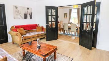 Uma sala de estar com um sofá, uma mesa de centro e uma porta aberta que dá para uma área de refeições.