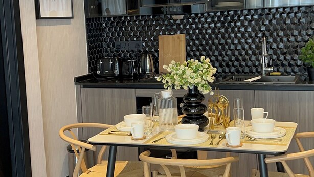 Uma cozinha moderna com painel de parede preto, armários de madeira e um espaço de refeições com mesa posta para quatro pessoas.